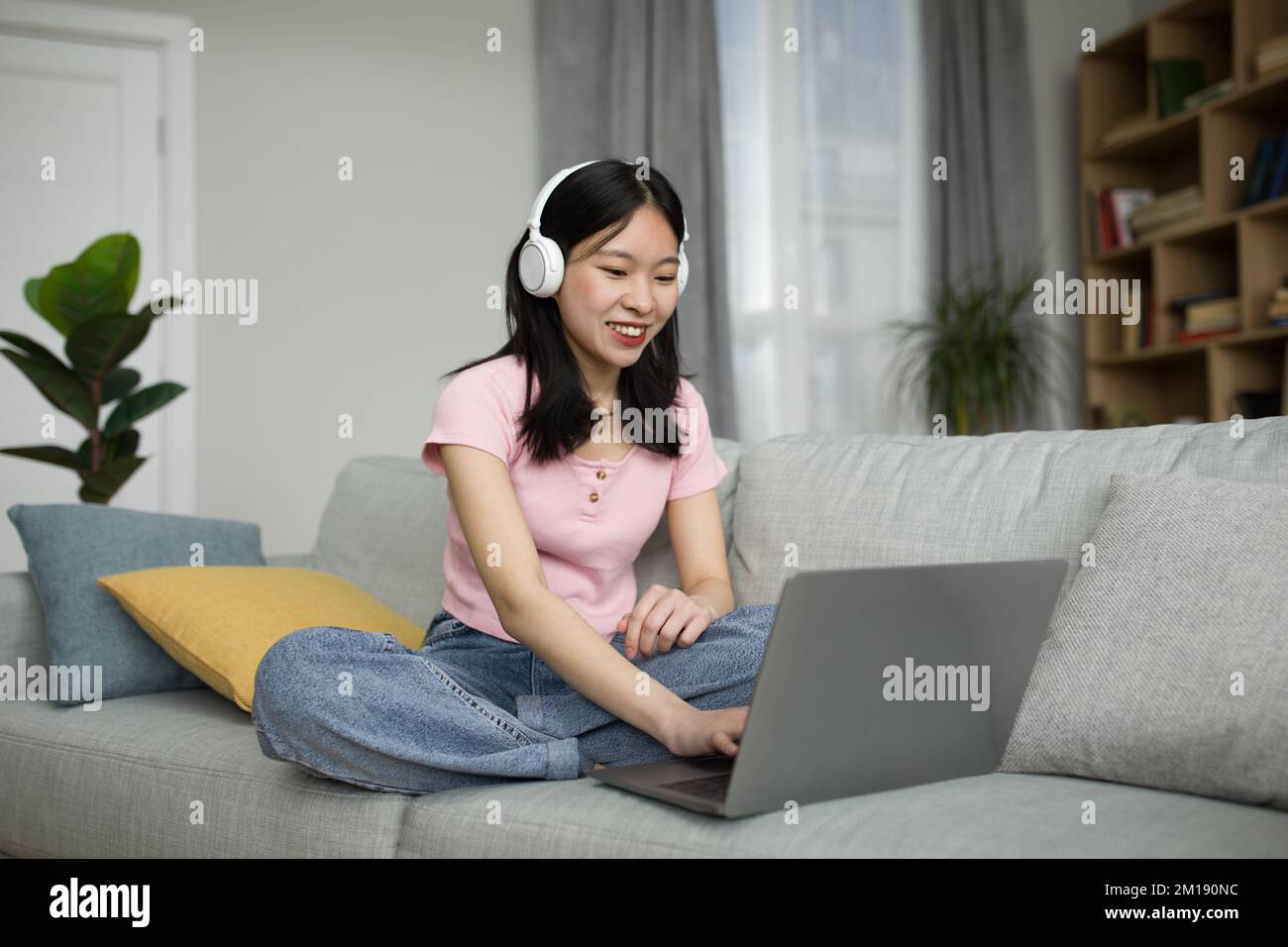 Young korean woman in headphones using laptop computer, working online ...