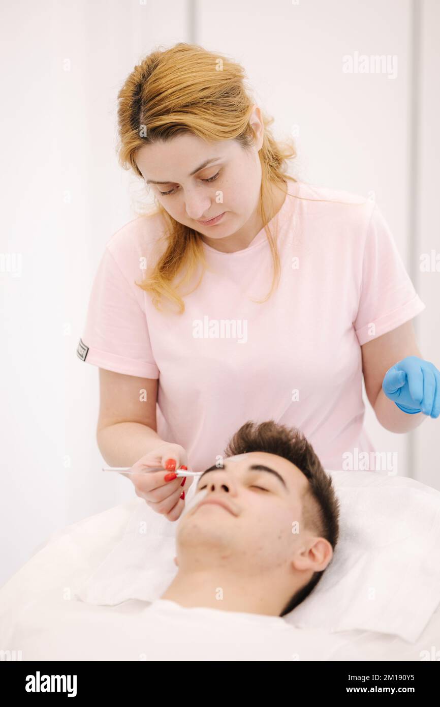 Cosmetologist applying clay mask on man's face in spa salon. Beautician ...