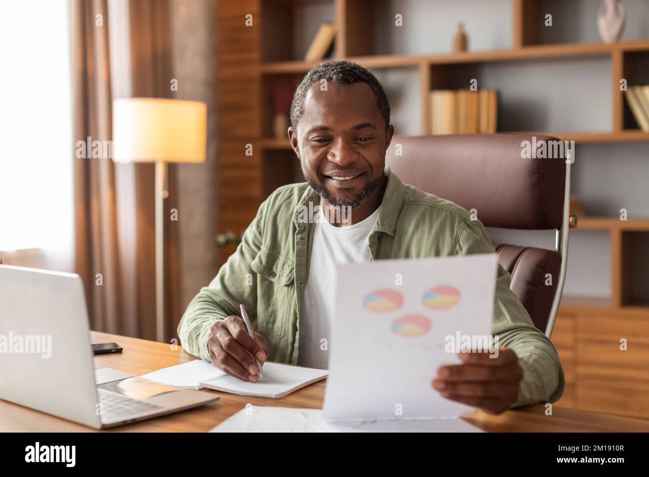 Cheerful busy middle aged black guy makes notes and works with graphs ...
