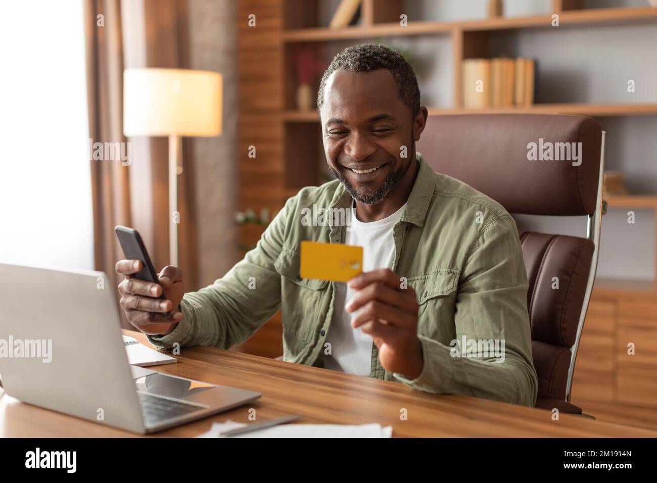 Glad mature black man uses credit card, laptop and phone to check ...