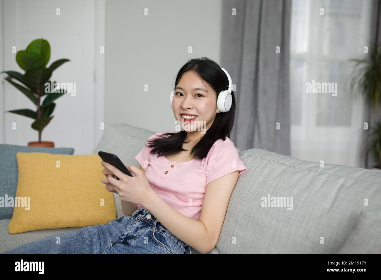 Happy japanese lady in headphones sitting on couch and listening to ...