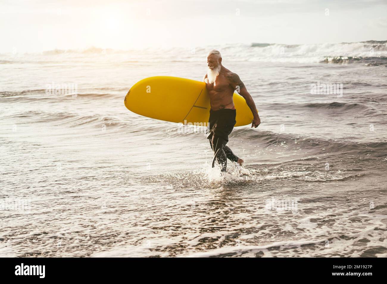 Senior surfer man walking on the beach after surf session at summer ...
