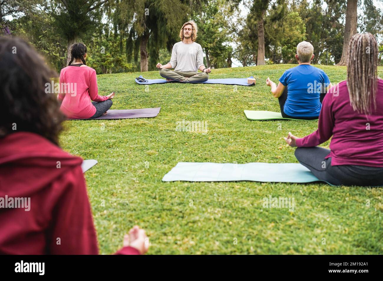 Multi generational people doing yoga meditation class at city park ...