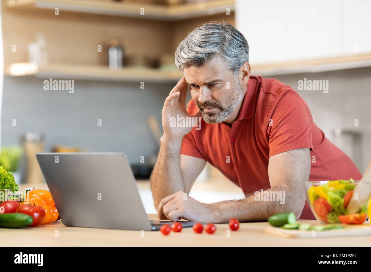 Stressed middle aged man looking at computer screen while cooking Stock ...