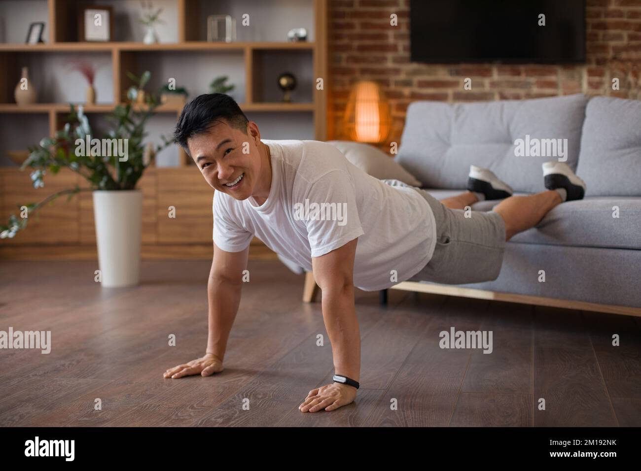 Strong middle aged asian man doing push ups with legs on sofa, working ...