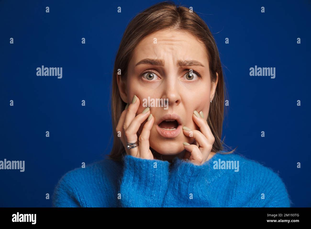 Young scared girl touching her cheeks with opened mouth over isolated ...
