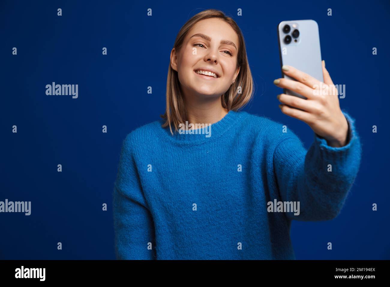 Young beautiful smiling happy girl taking selfie in blue sweater over ...