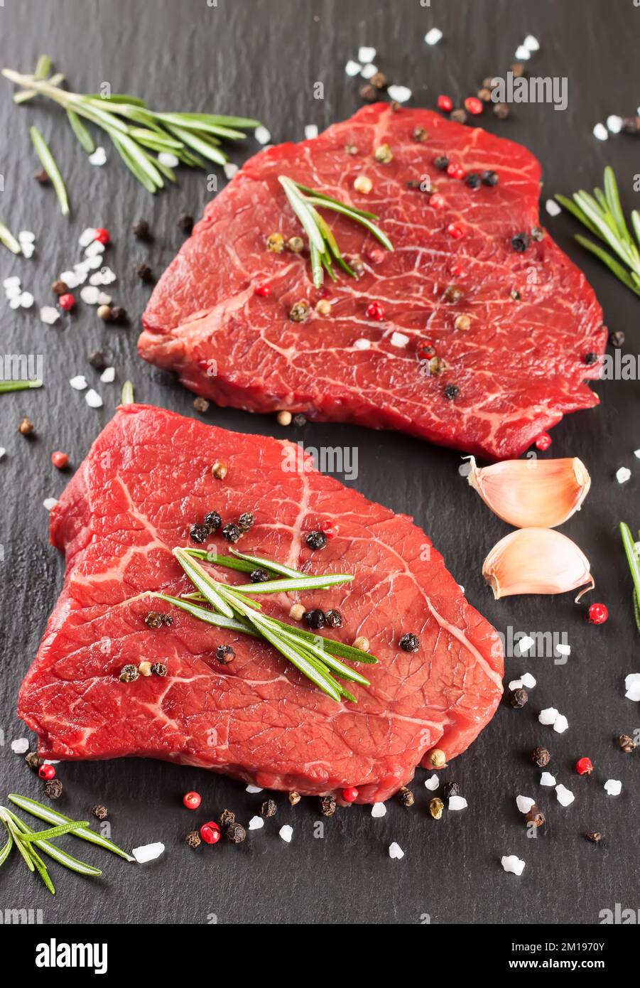 Raw beef steak with spices and ingredients for cooking on black slate ...