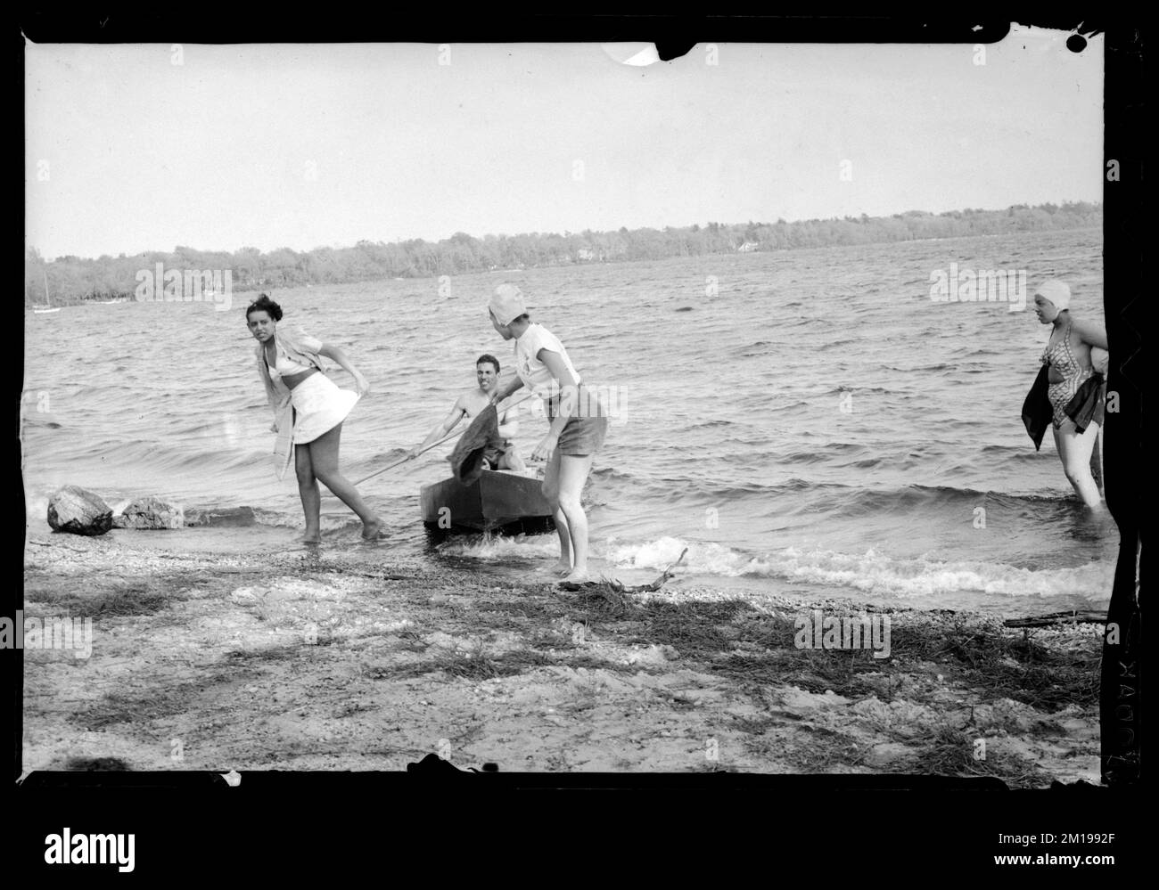 Three women walk out of the water while a man paddles his boat onto the ...