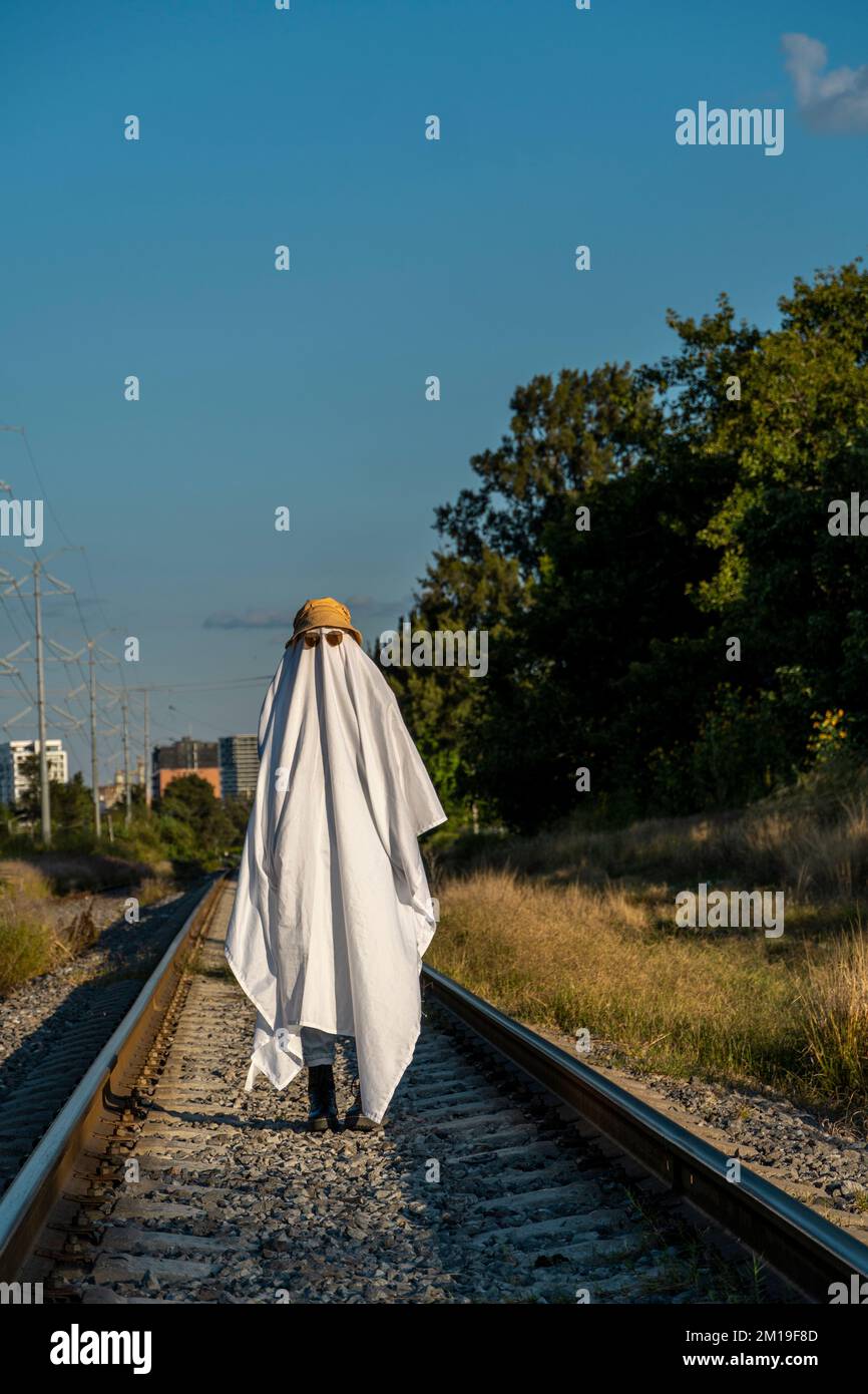 A vertical of a man covered with a white cloth looking like a ghost and ...