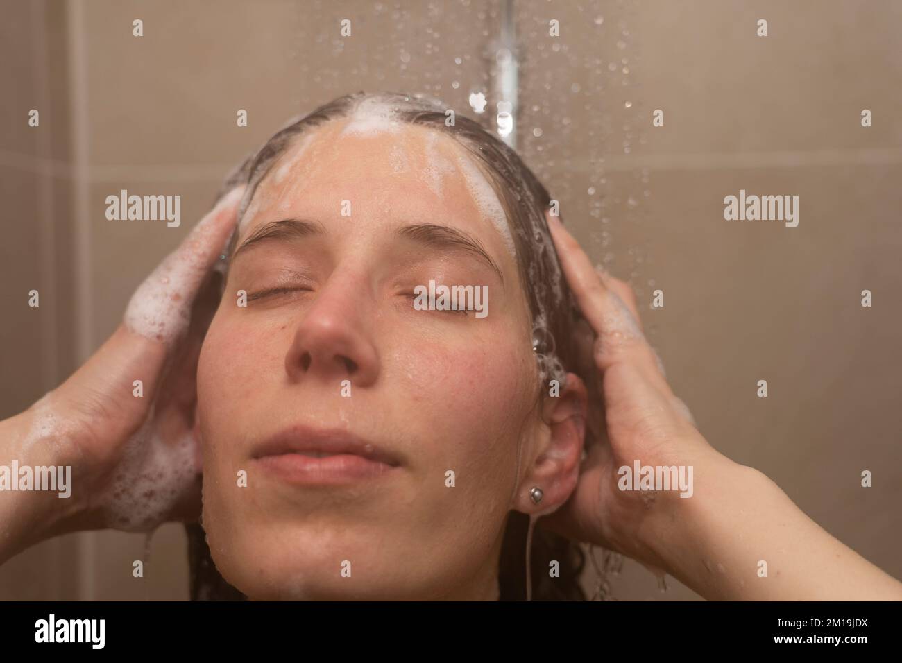 A woman in her thirties rinsing the shampoo out of her hair in t ...
