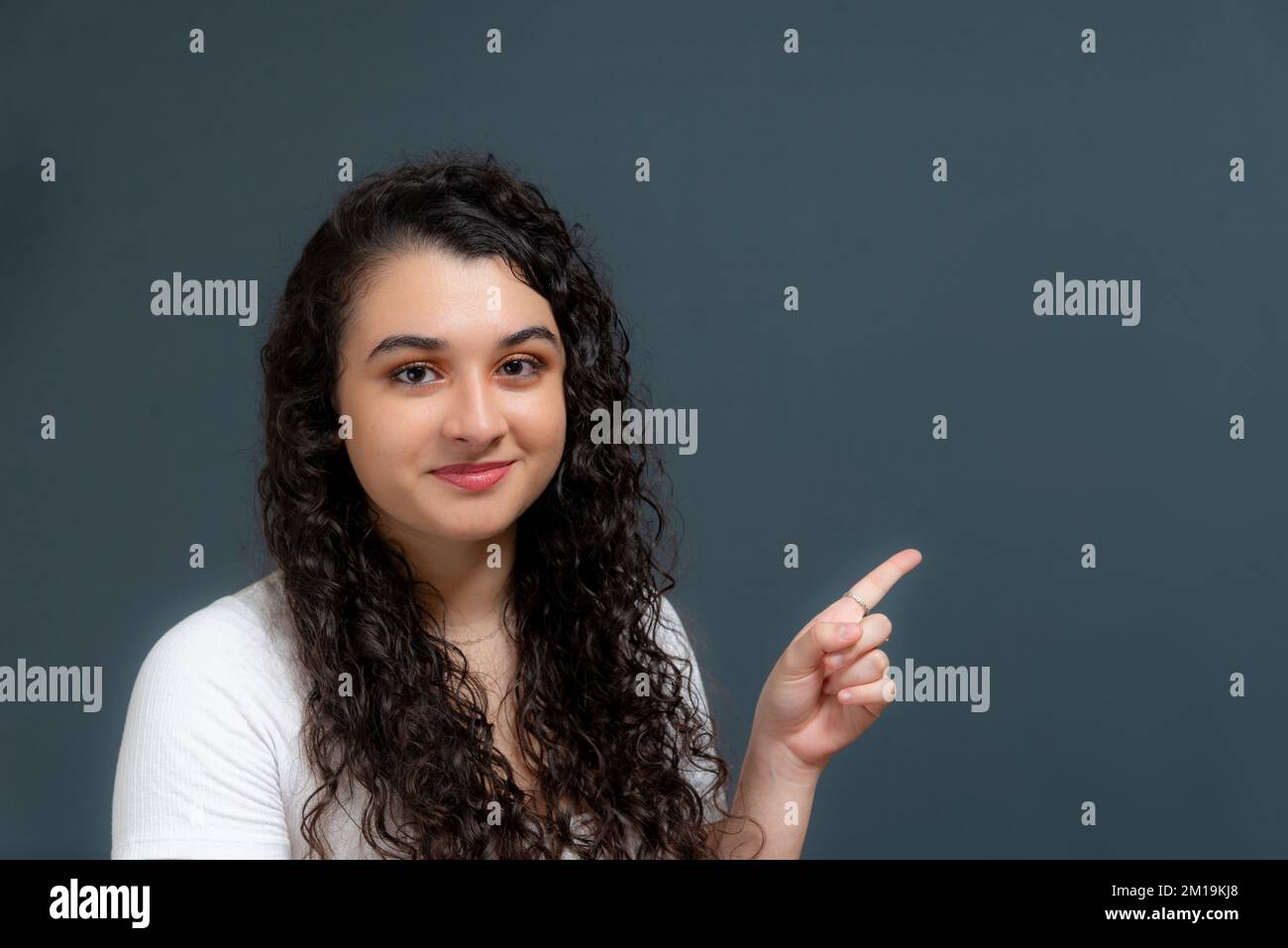 Portrait of young beautiful woman, pointing finger to the side, smiling ...