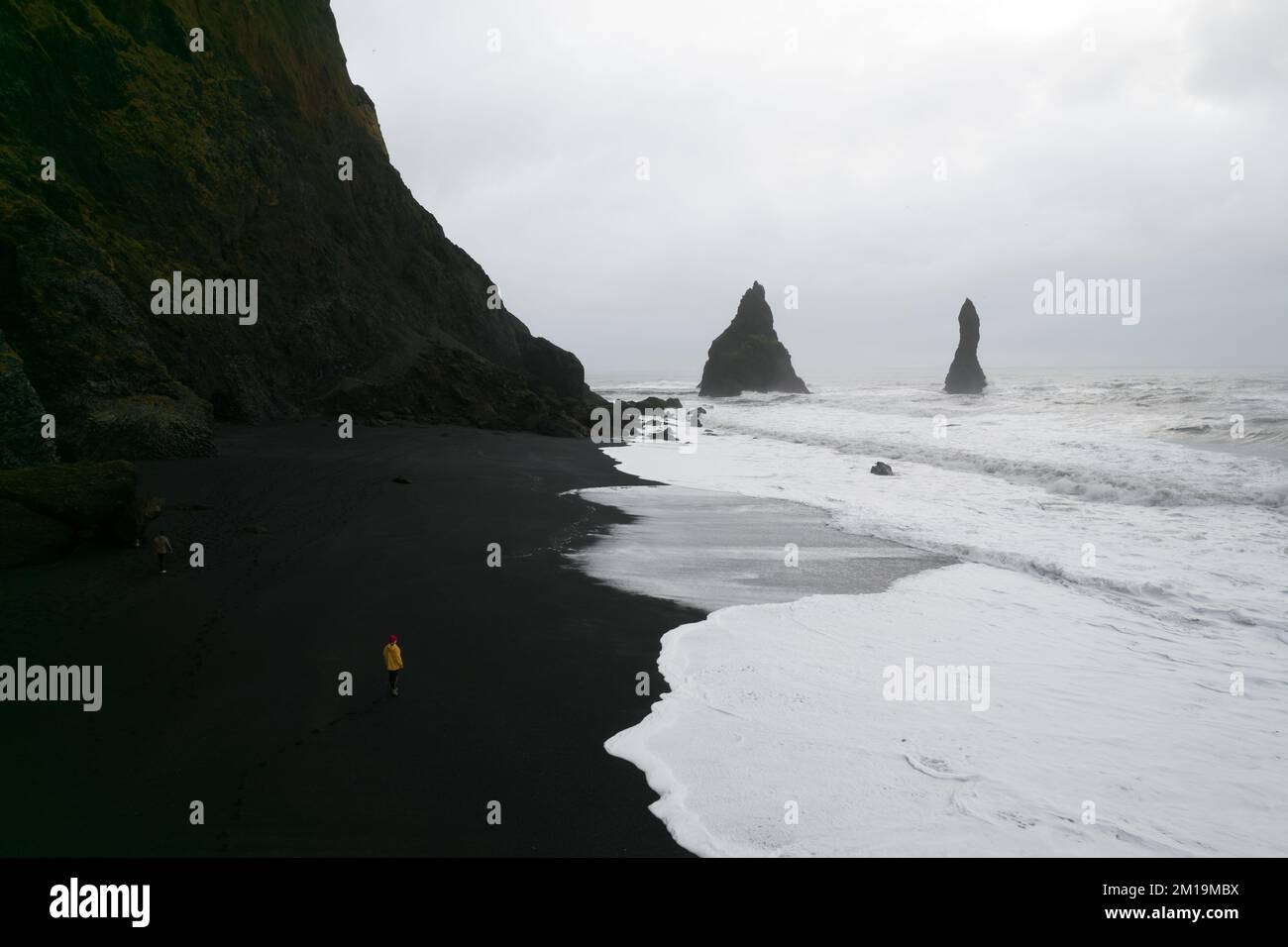 A woman in yellow jacket exploring black sand beach Reynisfjara in ...