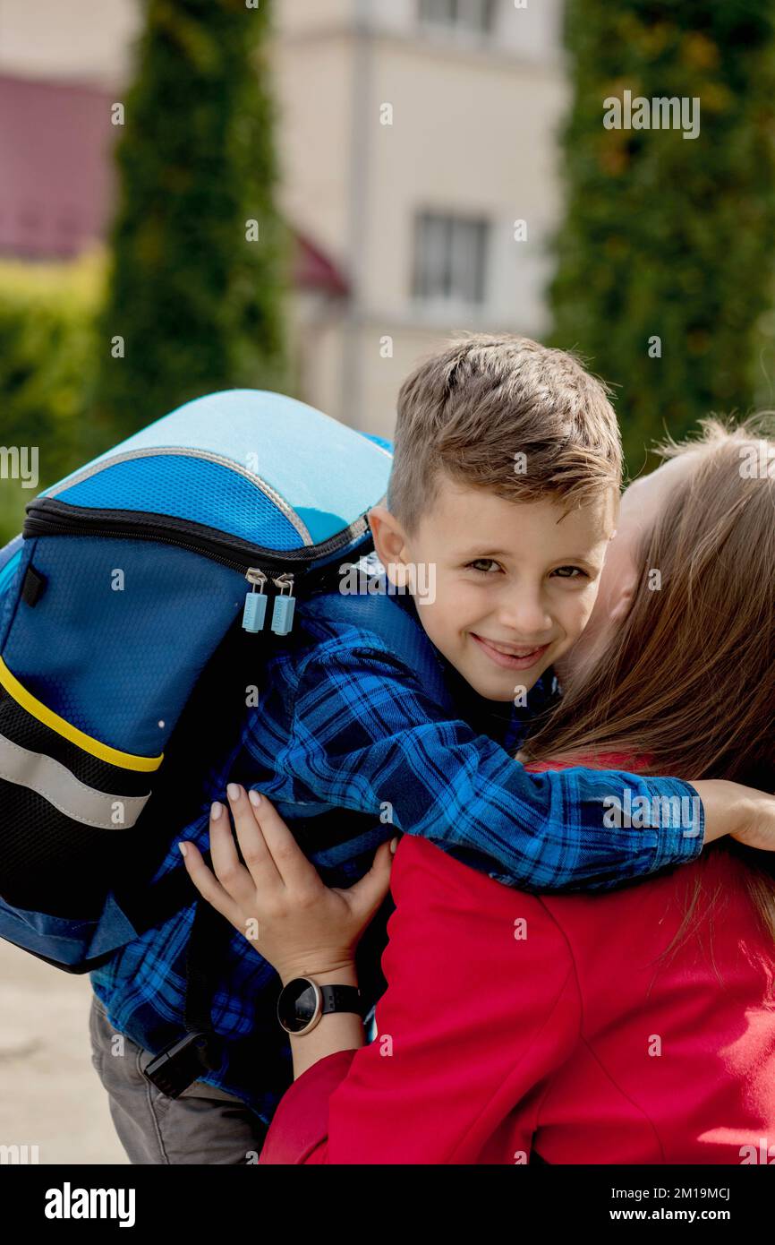 Young mother embraces her excited first class son on the way to school ...