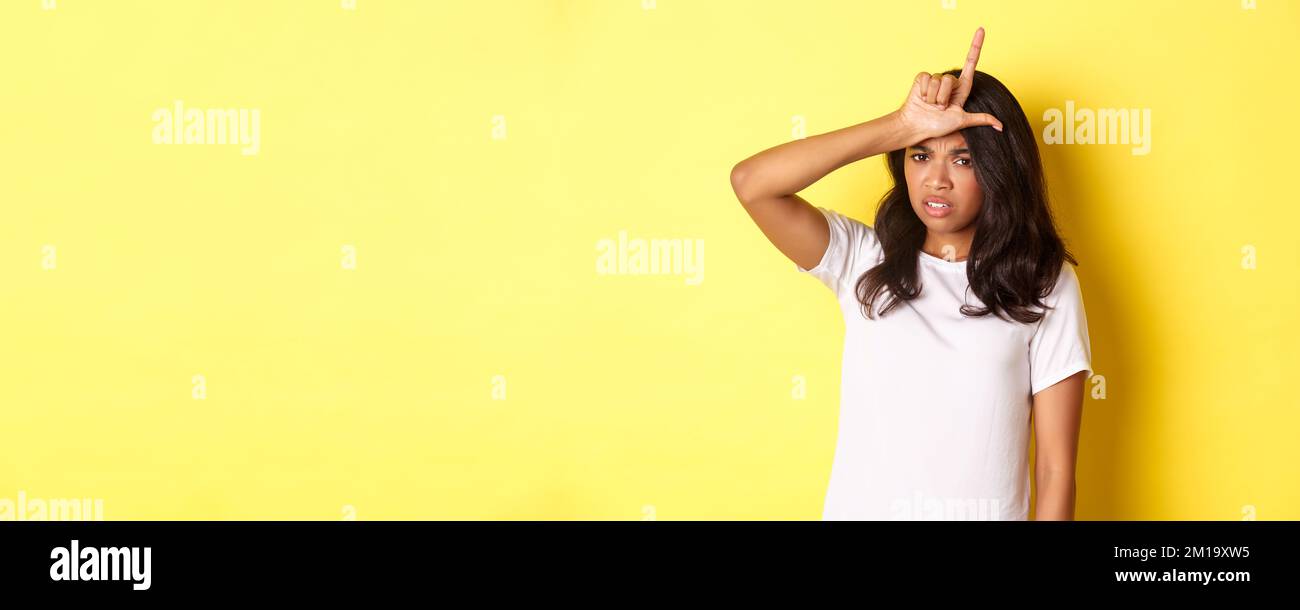 Image of sad african-american girl showing loser sign on forehead ...