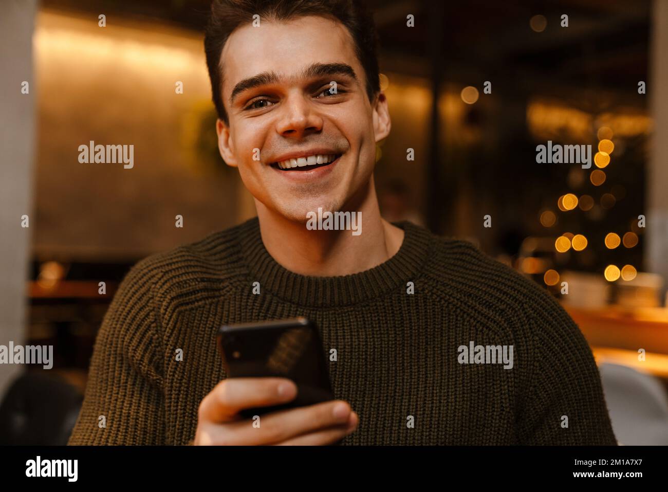 Young white brunette man wearing sweater smiling while using cellphone ...