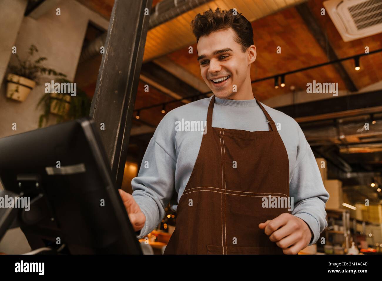 Young white waiter man wearing apron standing in front of computer and ...
