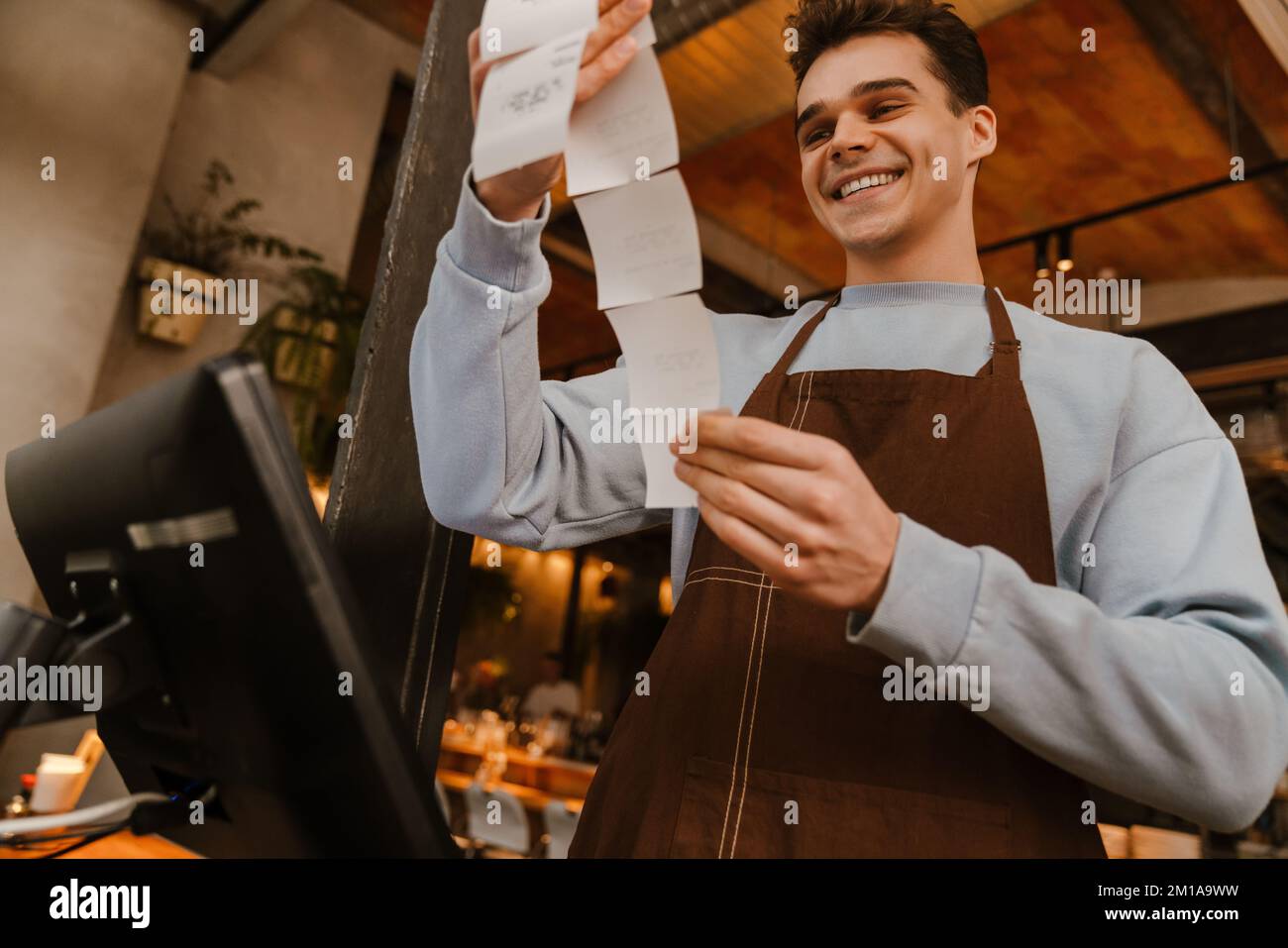 Young white waiter man wearing apron standing in front of computer and ...