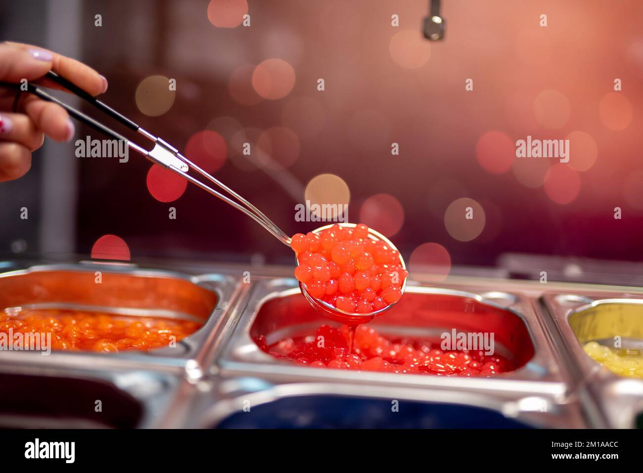 A closeup of a hand scoop orange roe Caviar food from displayed poles ...