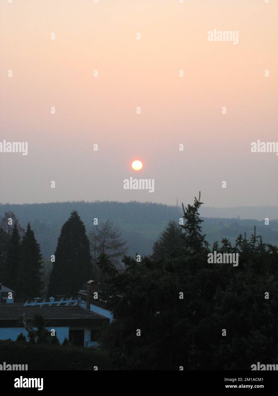 Low sun in a haze setting behind a hill Stock Photo - Alamy