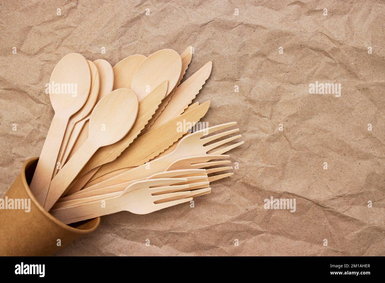 Wooden forks, spoons and knifes in cardboard cup on crumpled paper ...