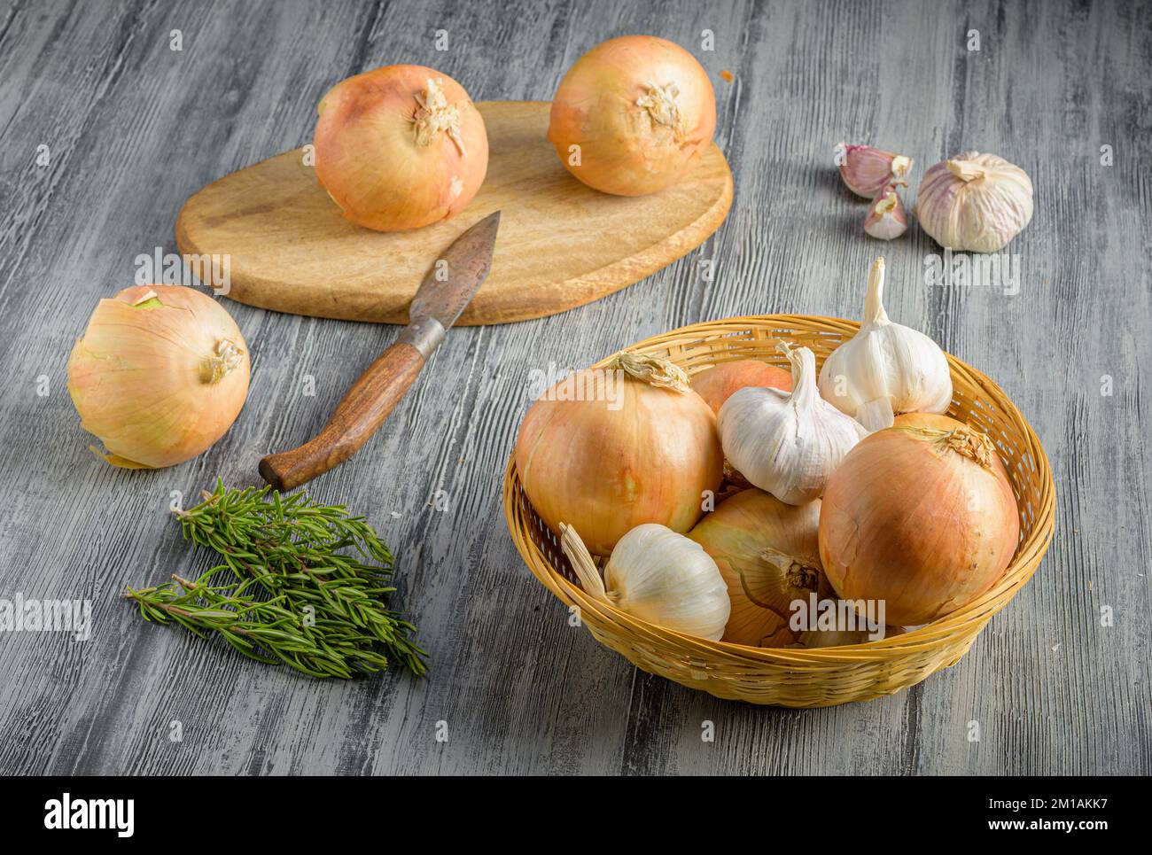 A beautiful shot of onions, garlic in a wicker basket, and rosemary ...