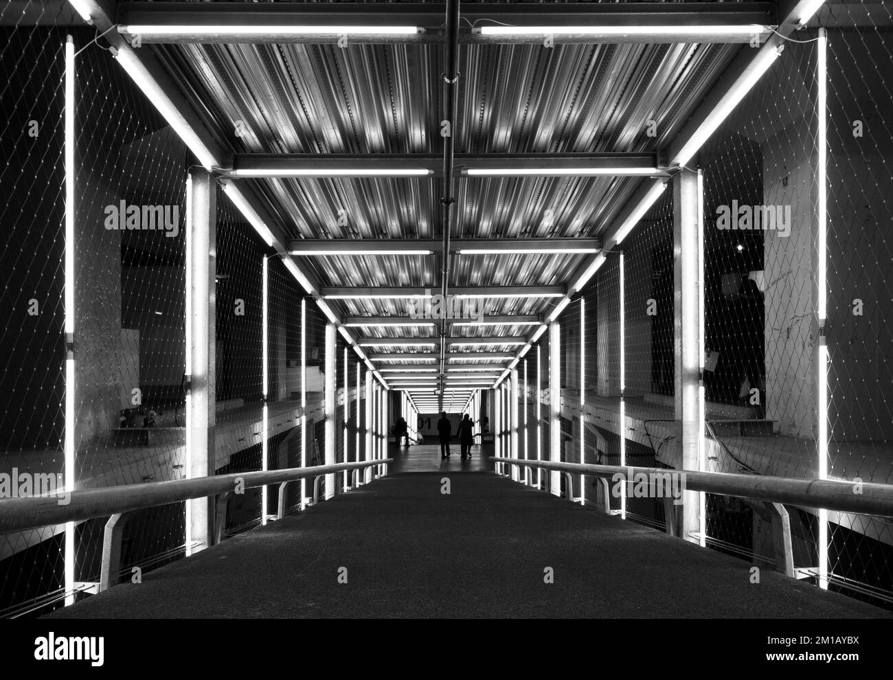 A grey shot of people walking on an asphalt underground road surrounded ...