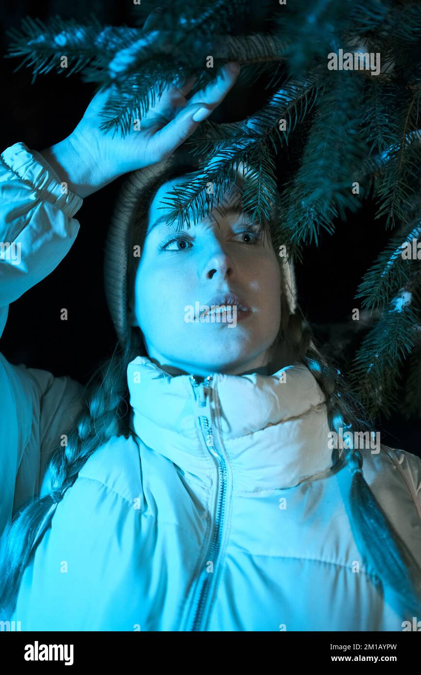 Young blonde girl with tails standing under spruce branches in the park ...