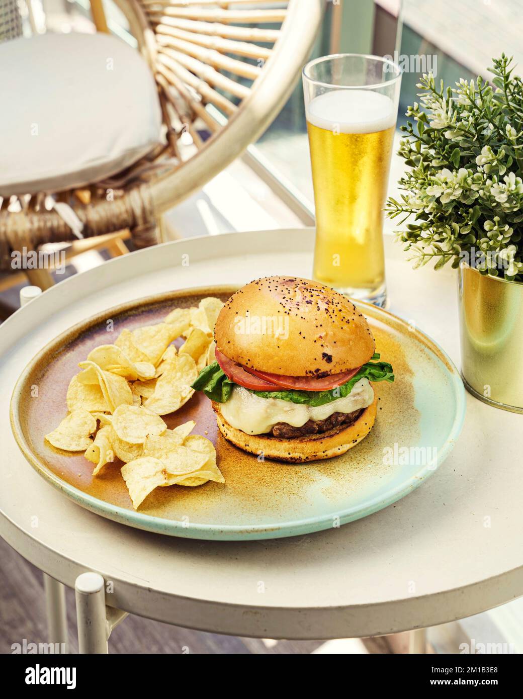 A closeup of a cheese burger with potato chips and a a glass of beer on ...
