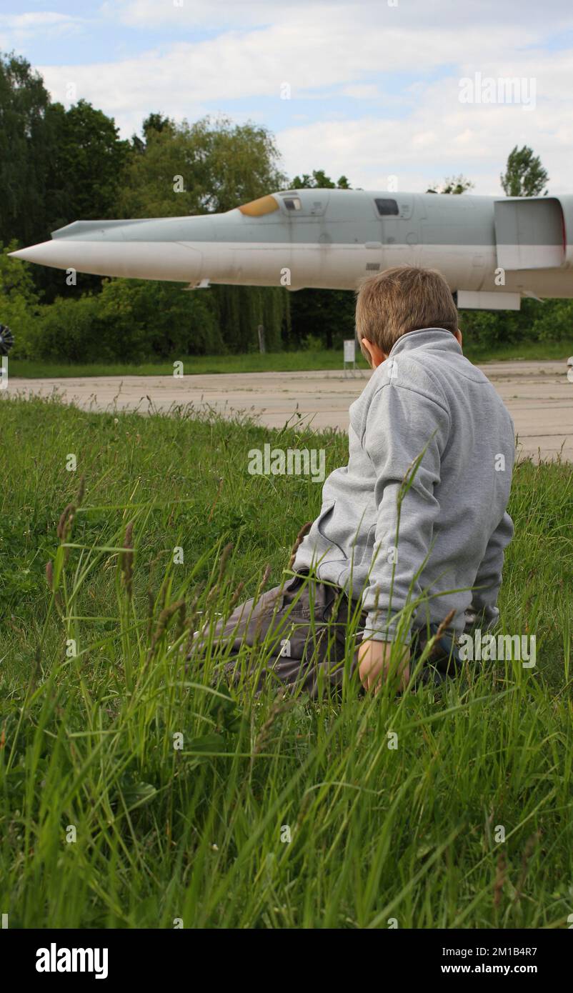 A little boy plays in the grass near a concrete ground with rockets ...