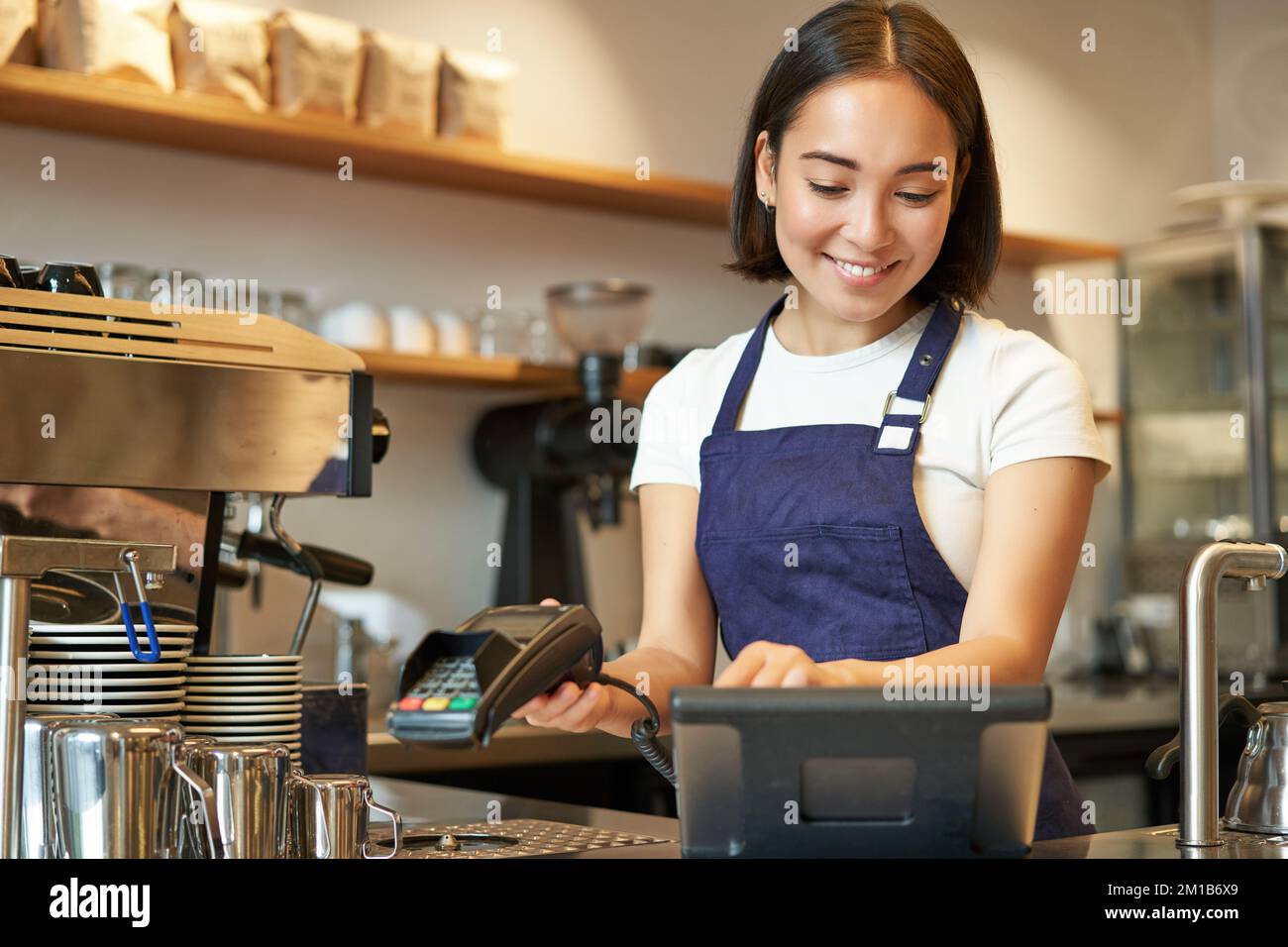 Smiling asian barista girl processing order, enter order in POS ...
