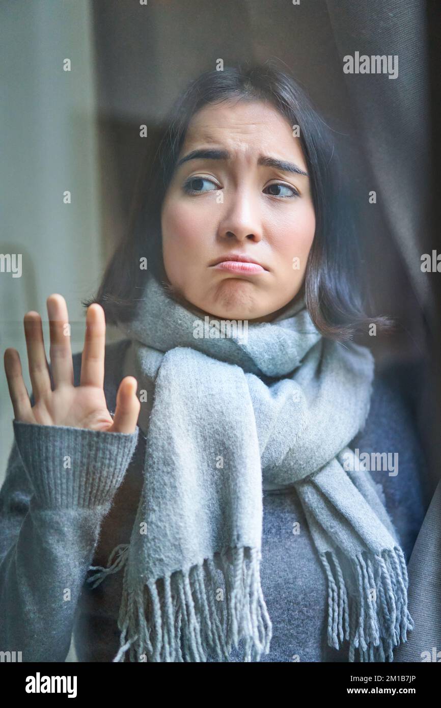 Vertical Shot Of Upset Asian Woman Looking Outside Touching Window