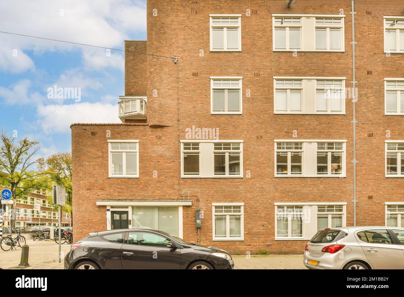 two cars parked in front of a tall brick building with white windows on ...