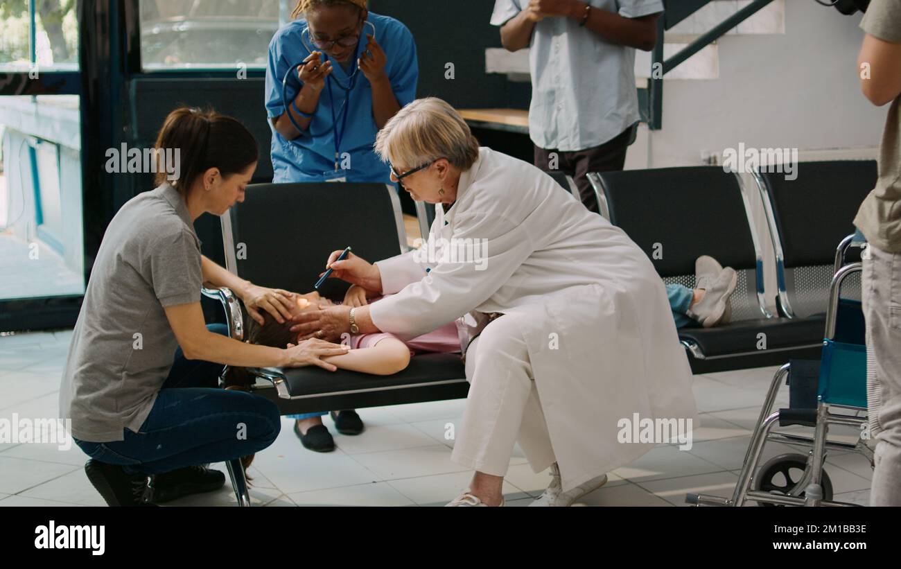 Elderly physician consulting small unconscious child with flashlight ...