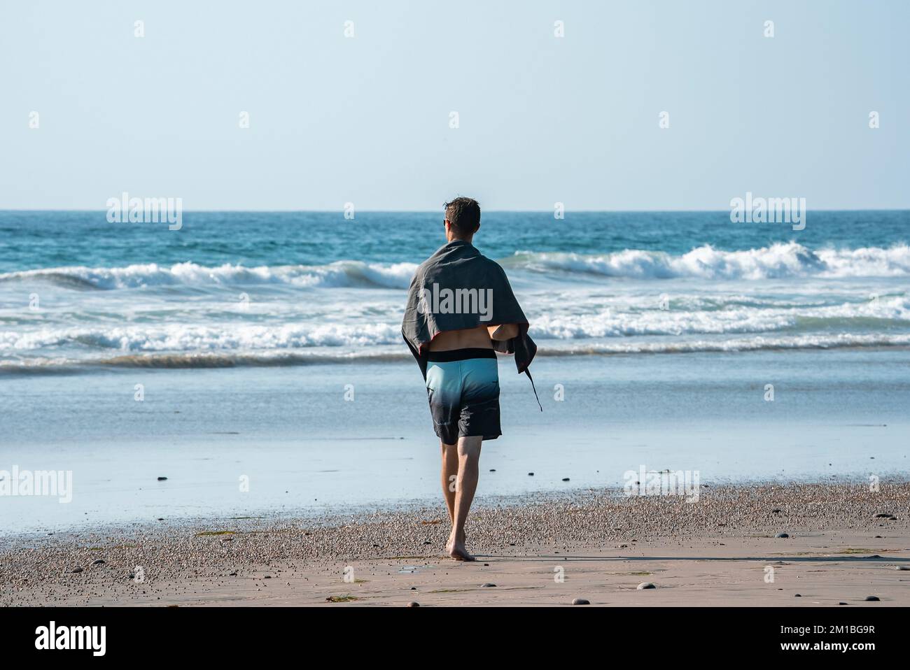 Rear view of man with towel walking at beach during summer Stock Photo ...