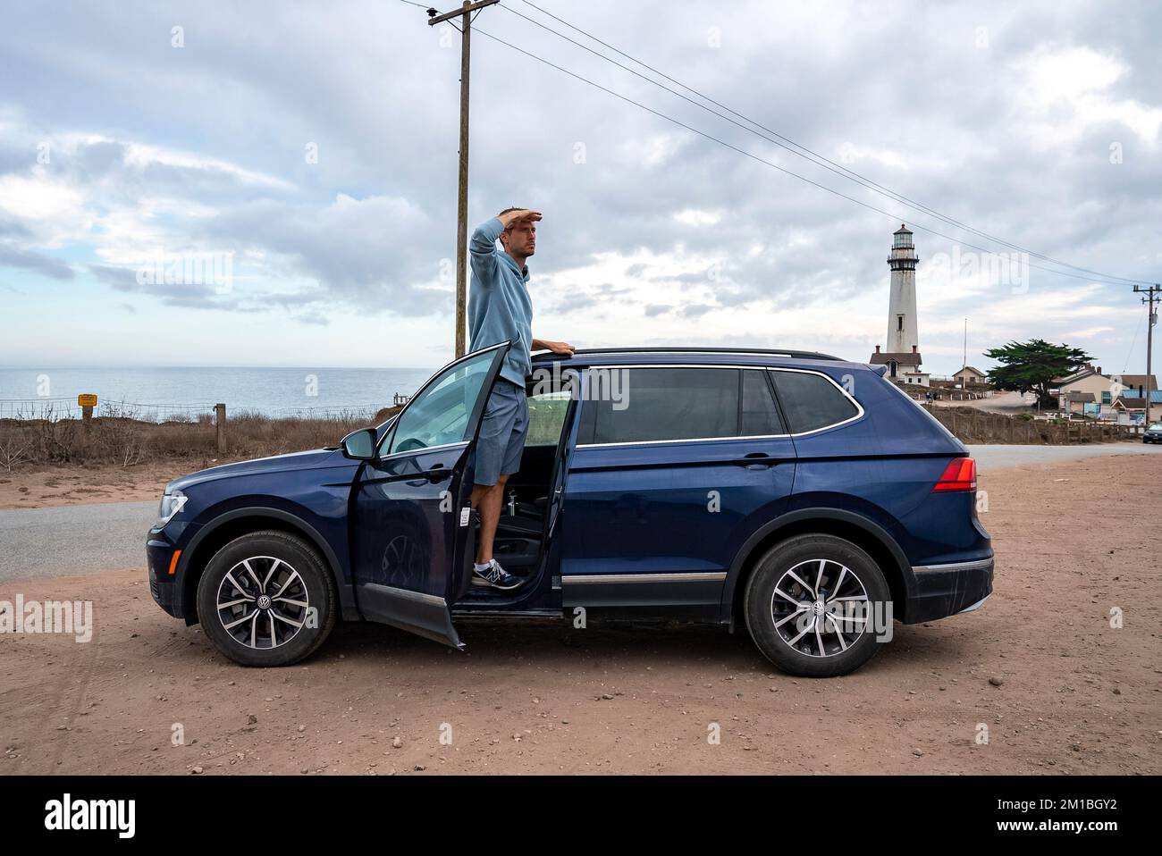 Man standing on car and looking away with Pigeon Point Lighthouse in ...