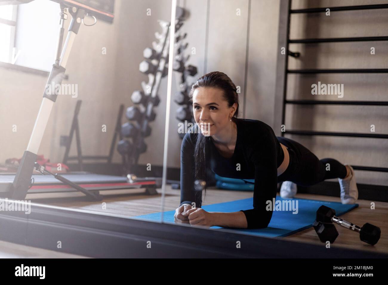 Beauty brunette woman standing in plank position in front of mirror at ...