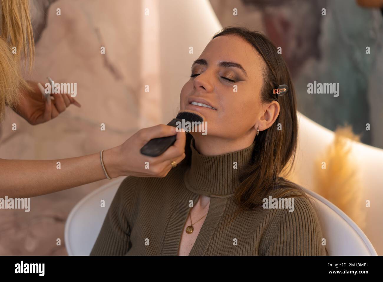 Crop makeup artist using soft brush to apply foundation cream on chin ...