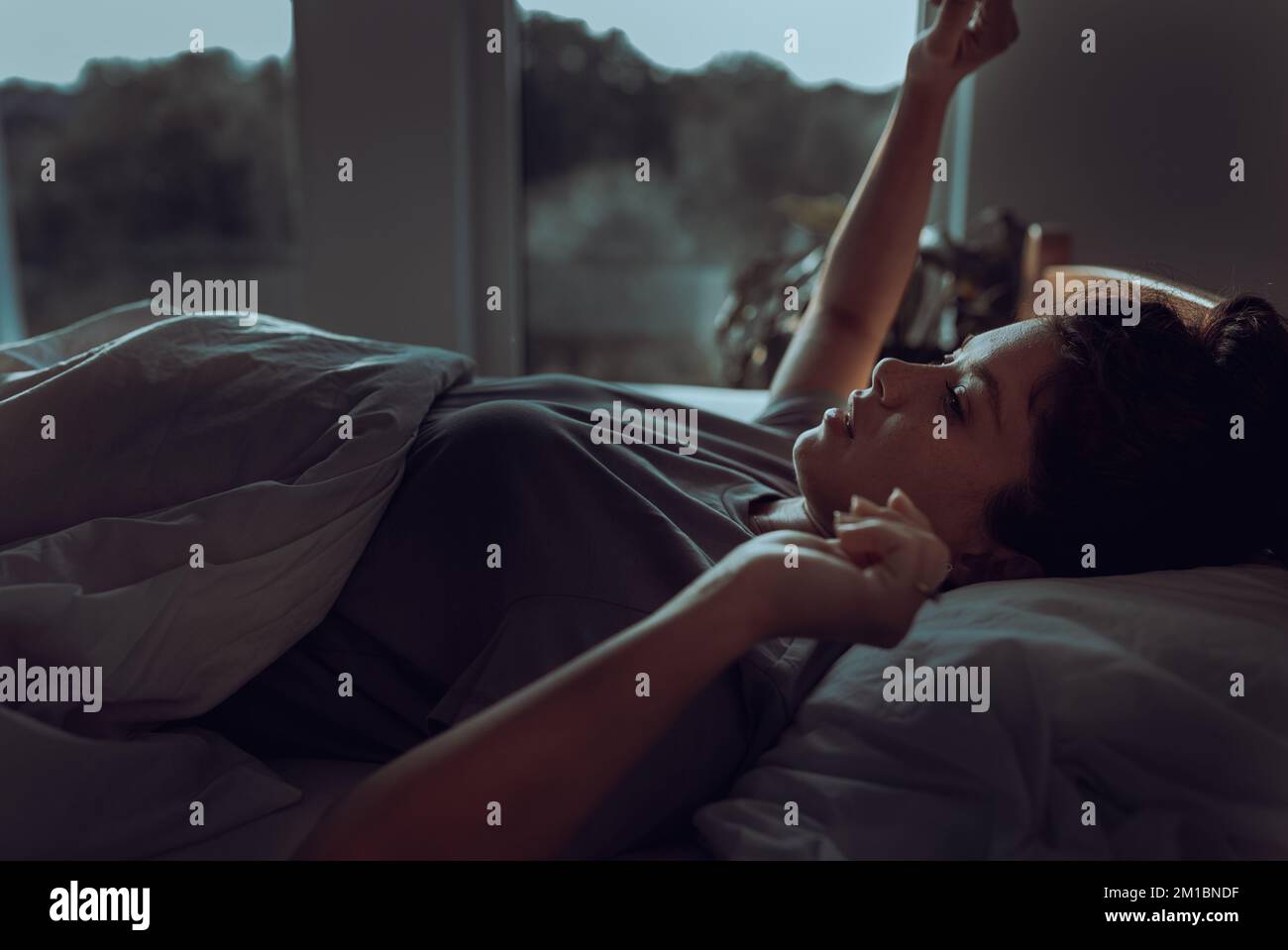 Young pretty woman waking up in bed in early morning with street light ...