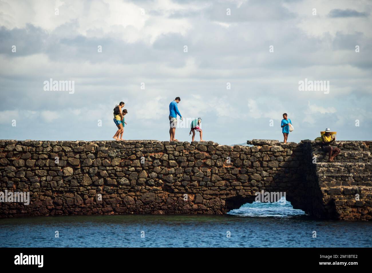 People walk on the stone breakwater of Porto da Barra beach in Salvador ...