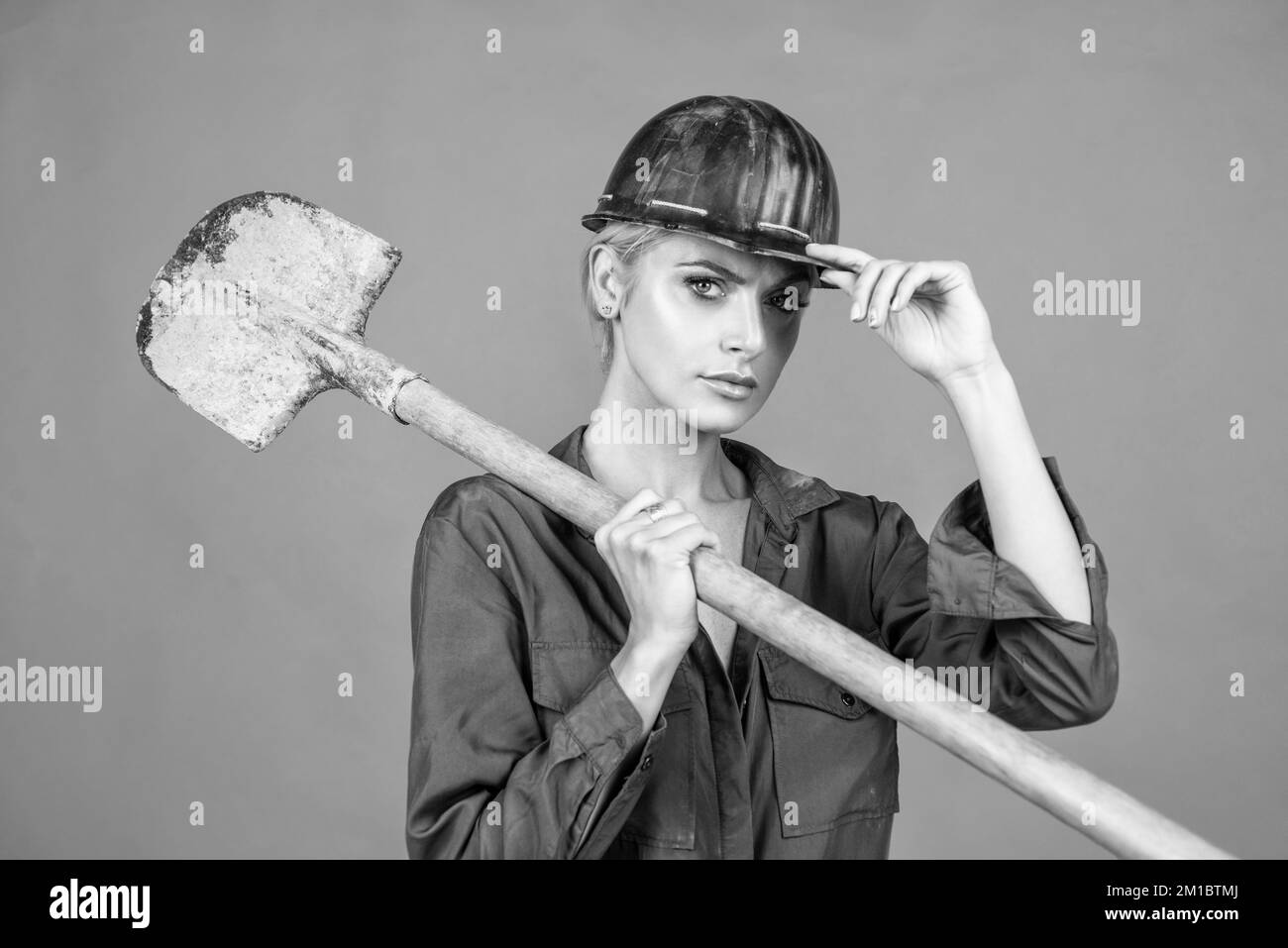 woman laborer in protective helmet and boilersuit hold shovel on orange ...