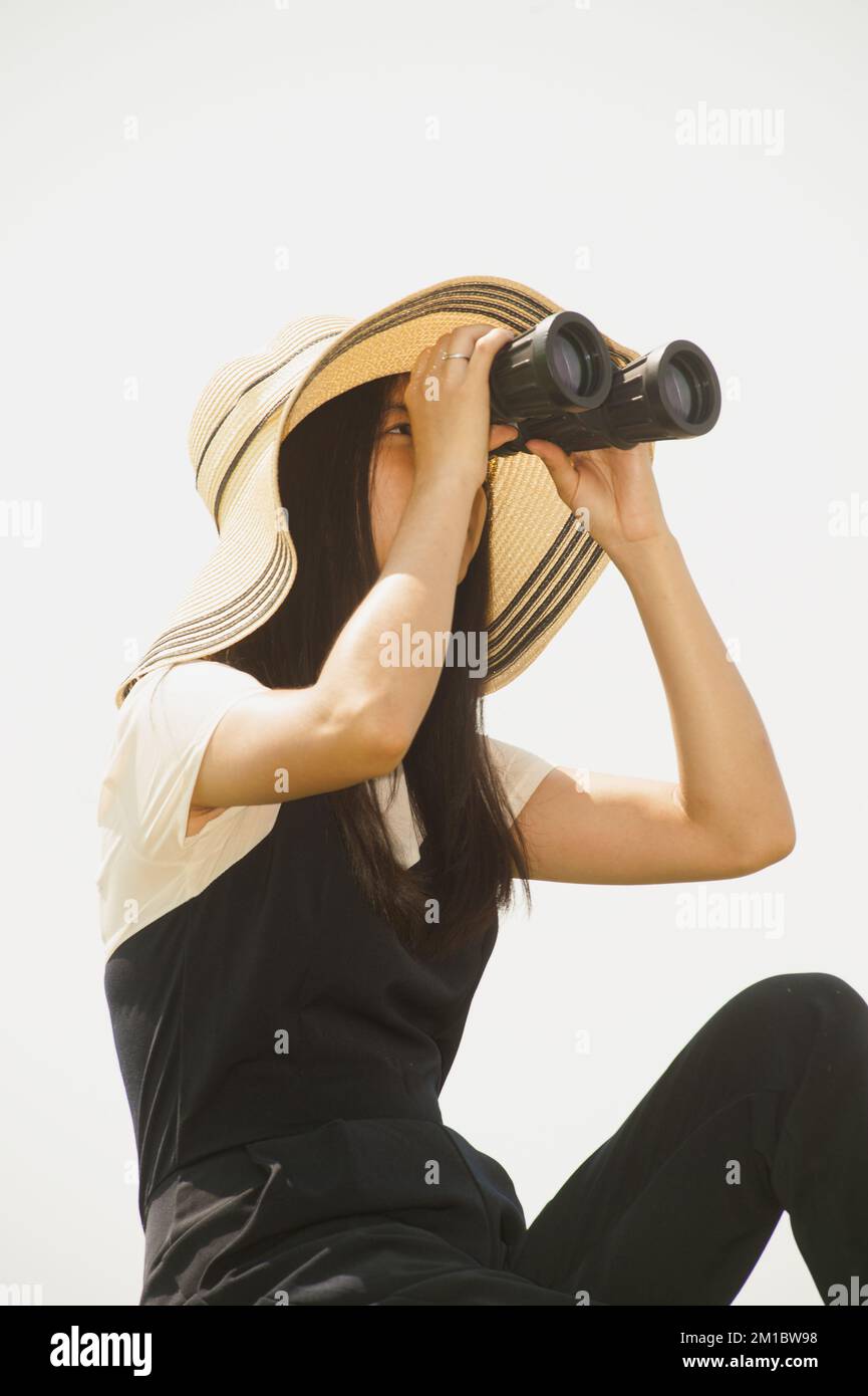 Pretty Asian young woman sit on mound seeking binoculars Stock Photo ...