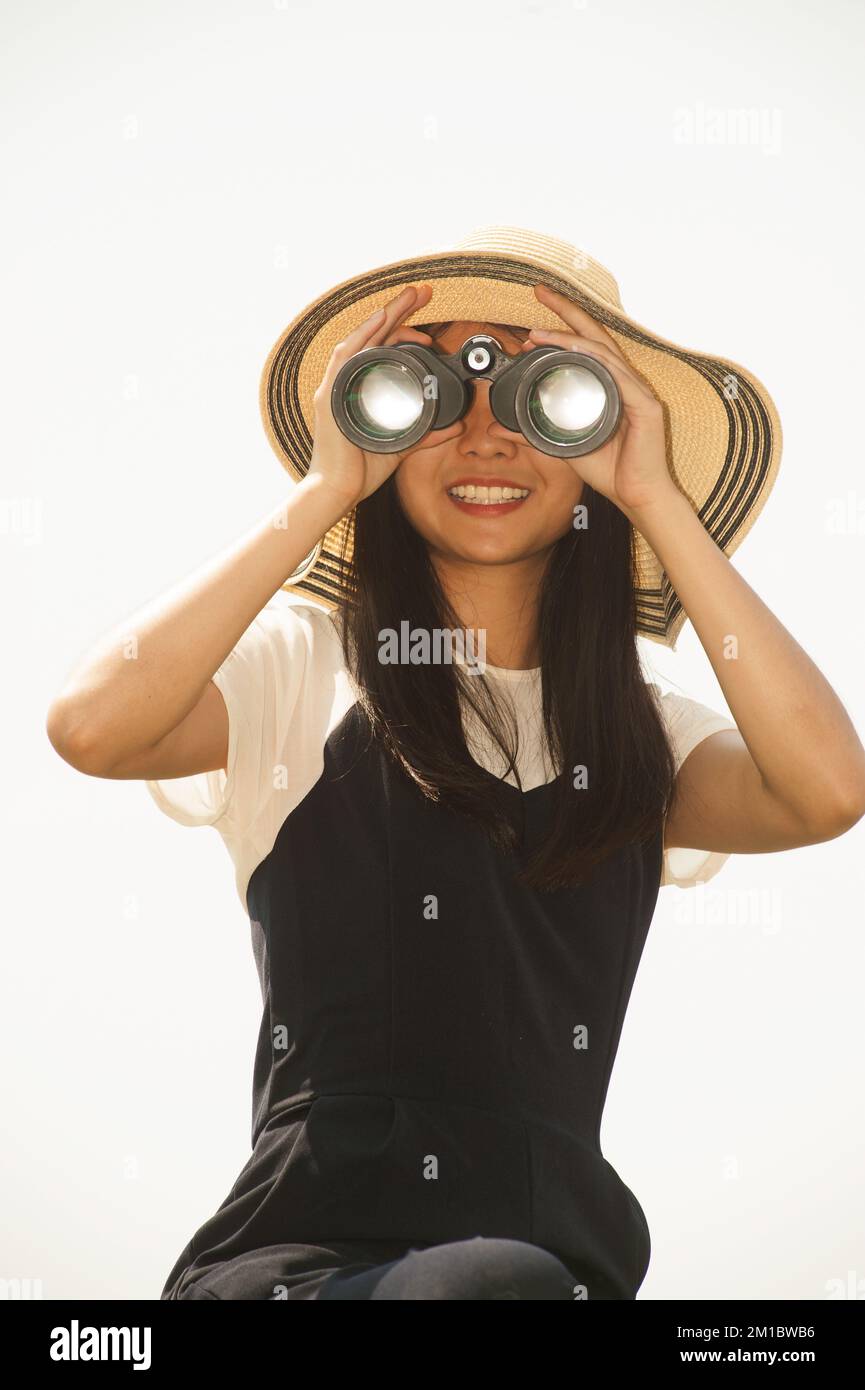 Pretty Asian young woman sit on mound seeking binoculars Stock Photo ...