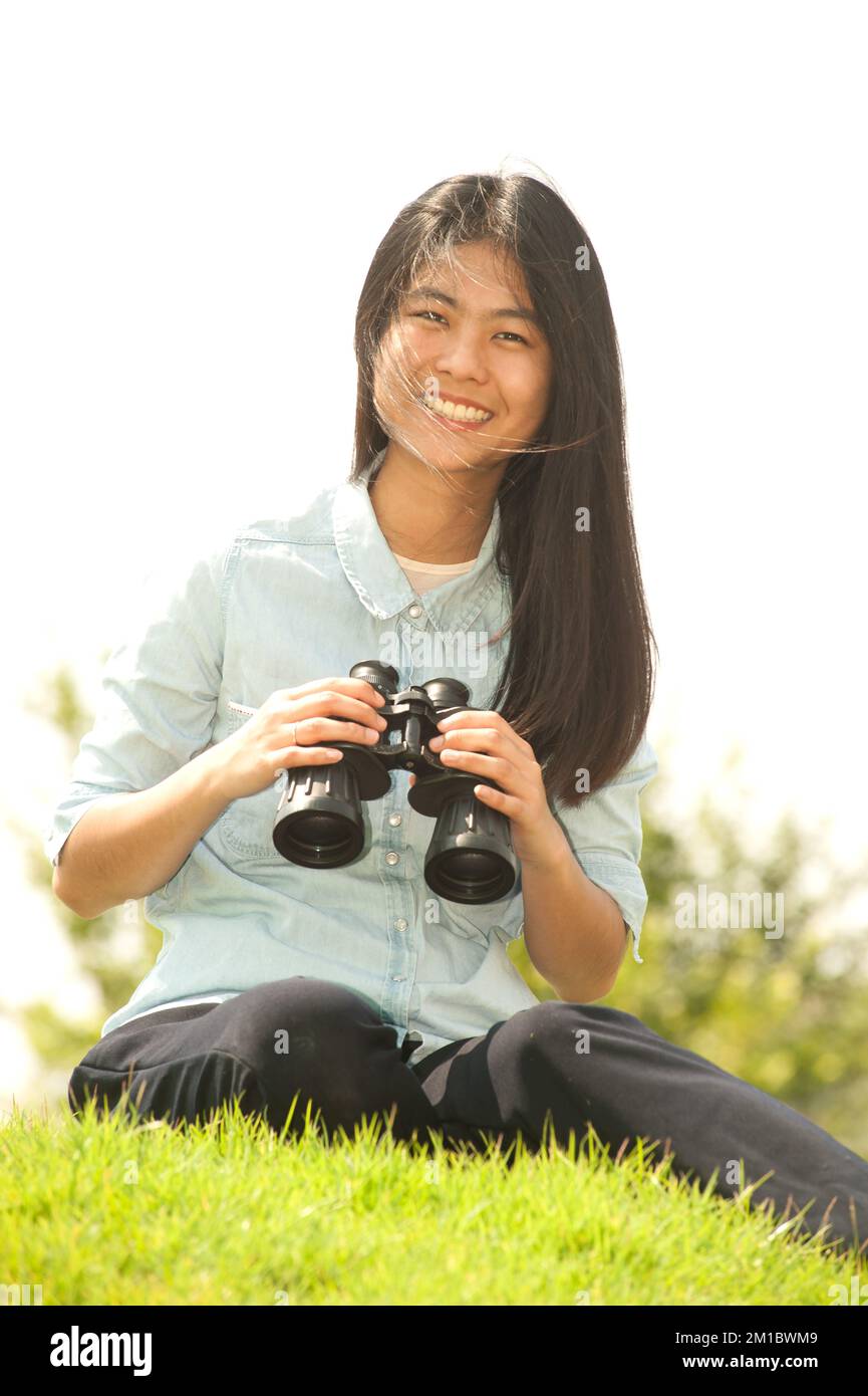 Pretty Asian young woman sit on mound seeking binoculars Stock Photo ...