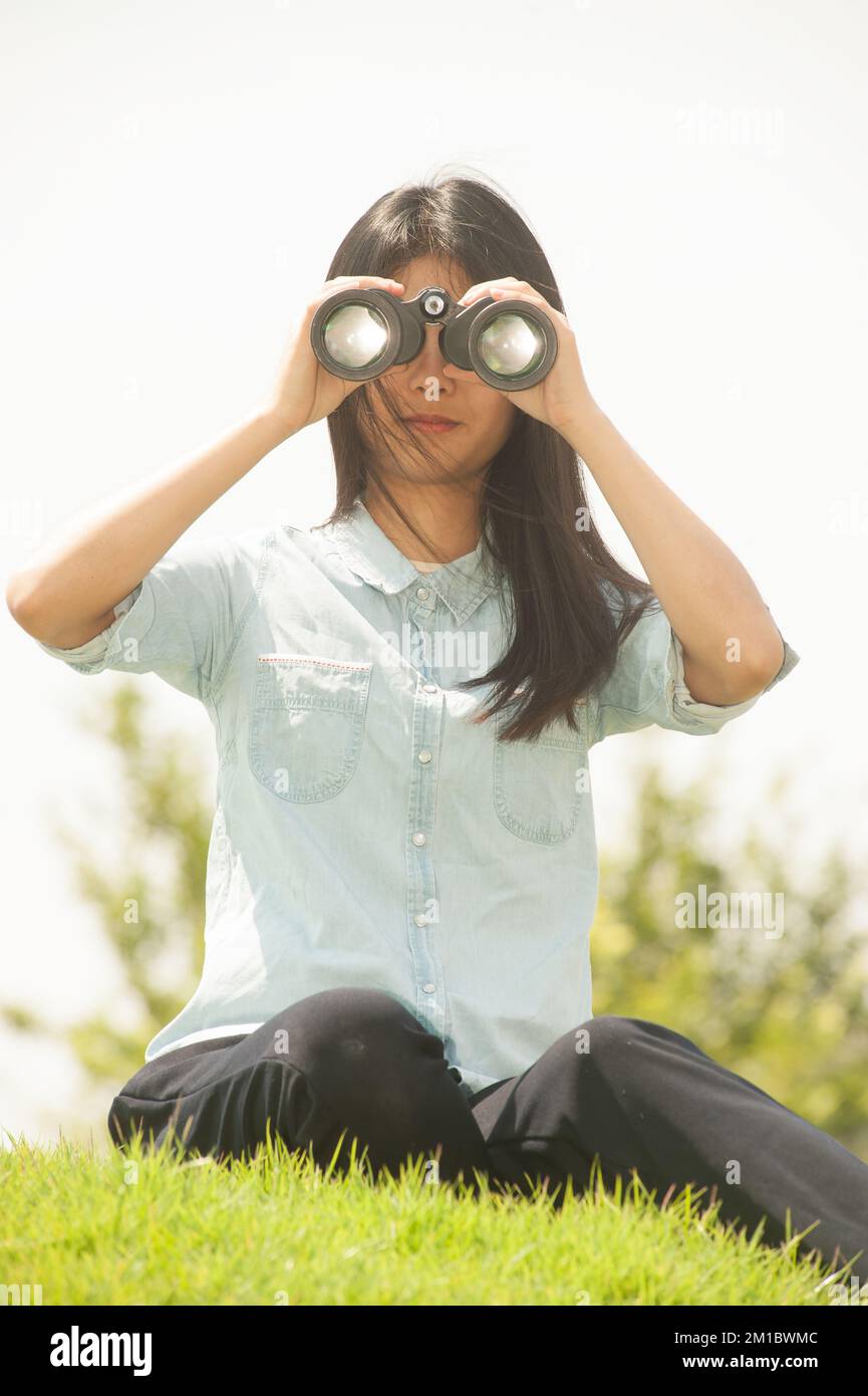 Pretty Asian young woman sit on mound seeking binoculars Stock Photo ...