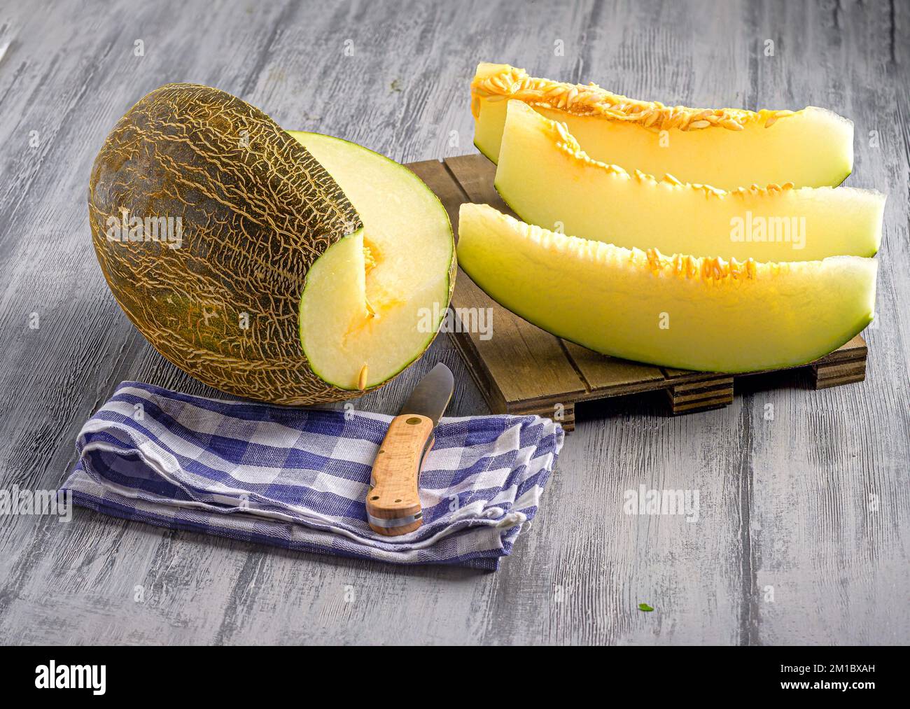 A closeup of almost whole melon and melon slices with knife on a wooden ...