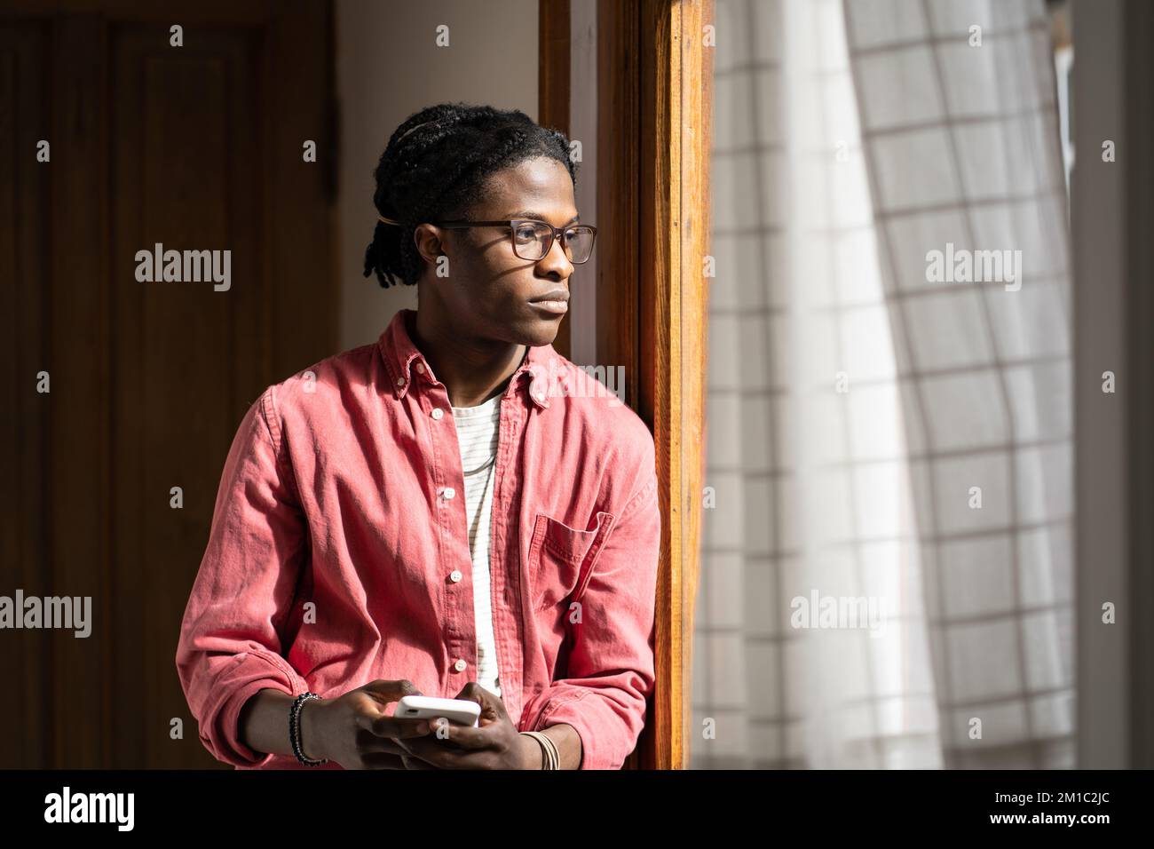 Pensive introverted African American man with mobile phone looking out ...