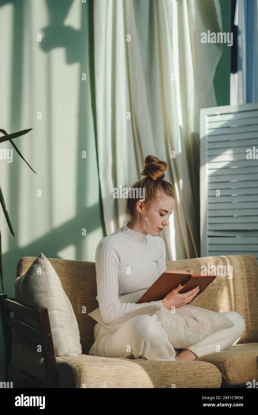 Beautiful young lady sitting on the couch, having fun while reading a ...
