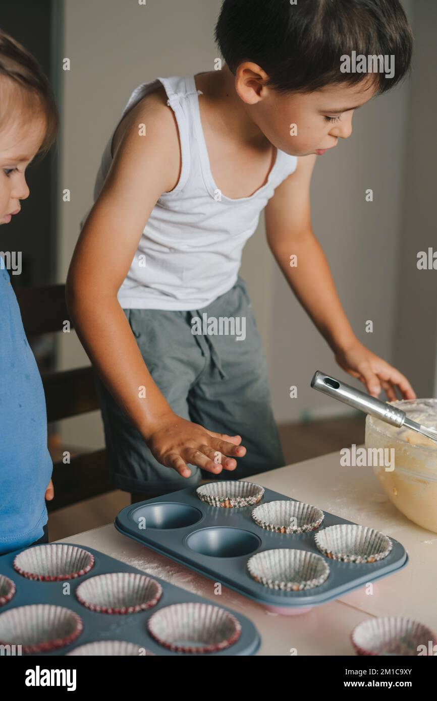 Happy son with her sister pouring dough in baking form. Son preparing ...