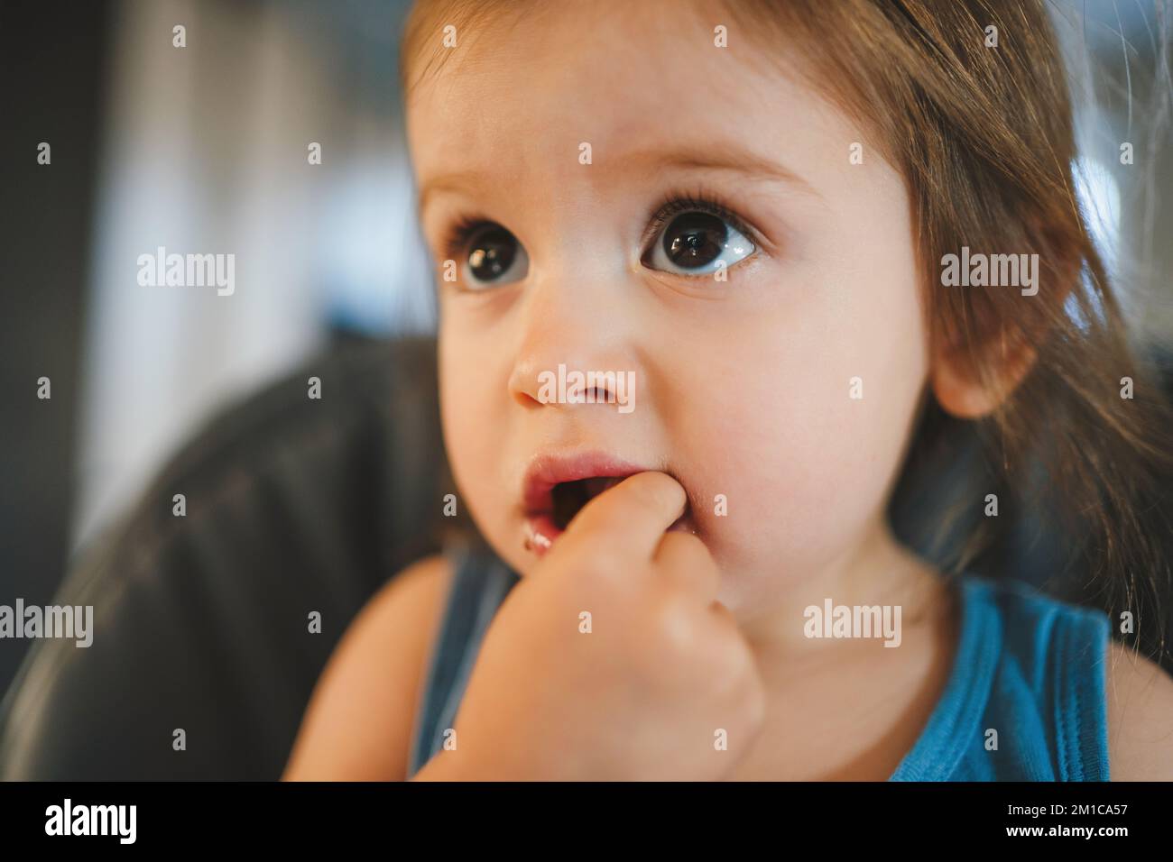 Close-up portrait of a little girl holding her fingers in her mouth ...